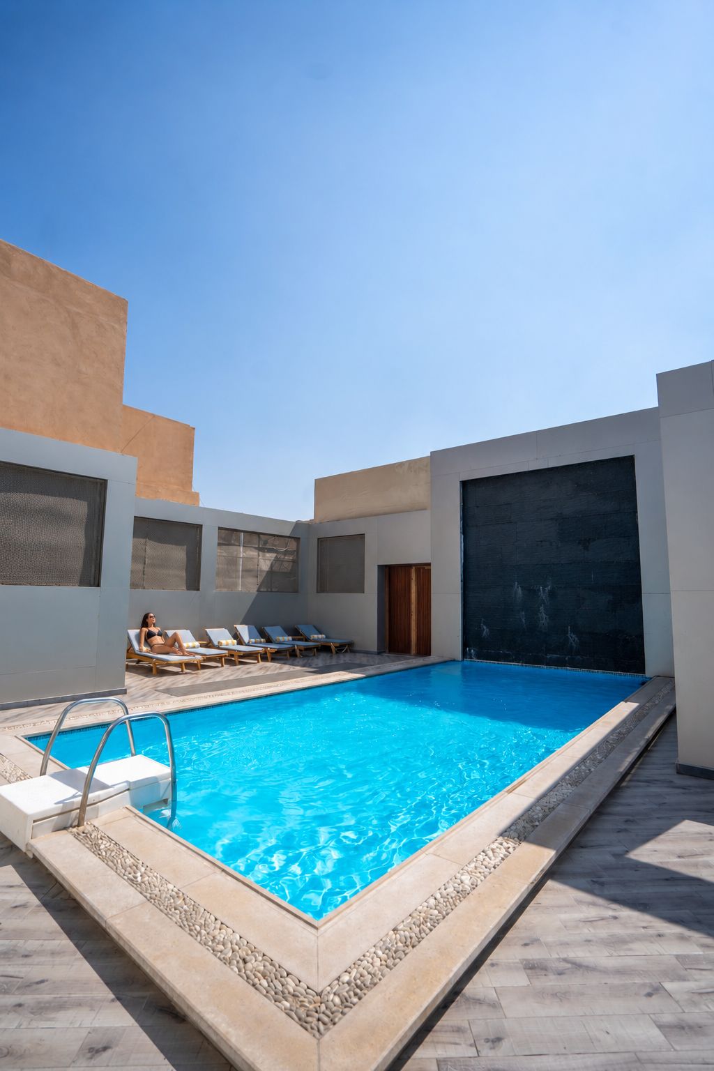Piscina moderna ao ar livre com espreguiçadeiras e céu azul límpido.