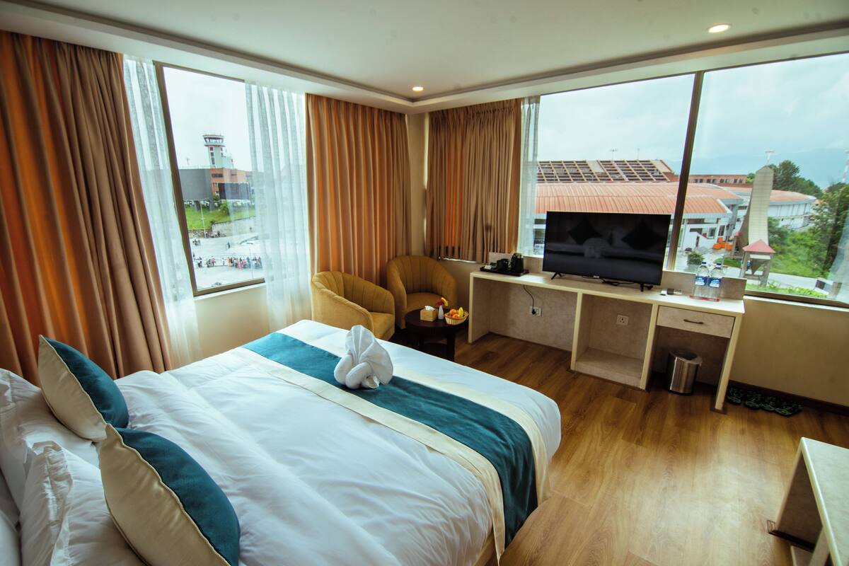 Quarto de hotel com uma cama grande, uma escrivaninha com televisão e vista para a cidade.