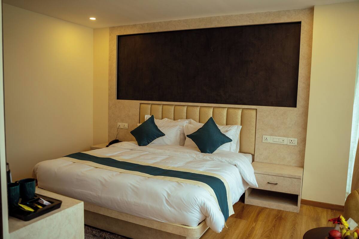 Quarto de hotel com uma cama grande, cabeceira, mesas de cabeceira e uma pequena escrivaninha com cadeira.