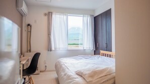 Quarto com cama, escrivaninha, cadeira e janela com cortinas.