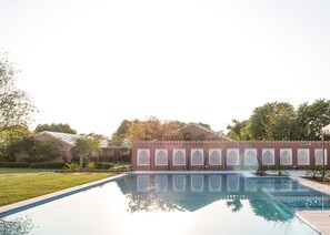 Piscina cercada por vegetação e árvores, com grade decorativa.