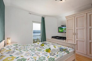 Quarto com cama, televisão, guarda-roupa e vista para o mar.