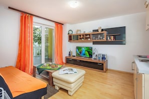 Uma sala de estar moderna com sofá, banquinho, televisão, estante de livros e área de jantar com mesa e cadeiras.