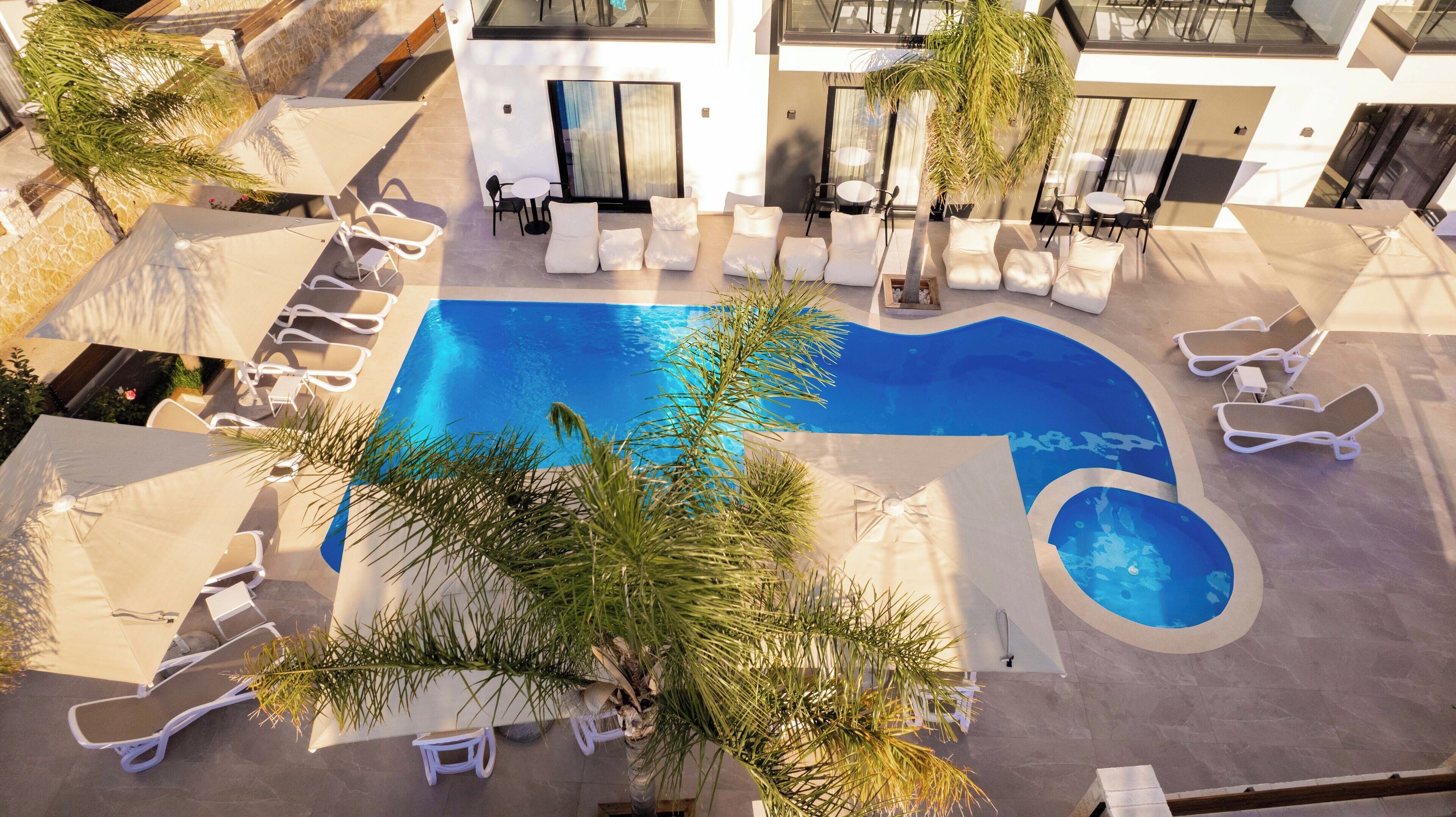 Vista aérea de uma área de piscina de hotel com espreguiçadeiras, piscina e palmeiras.