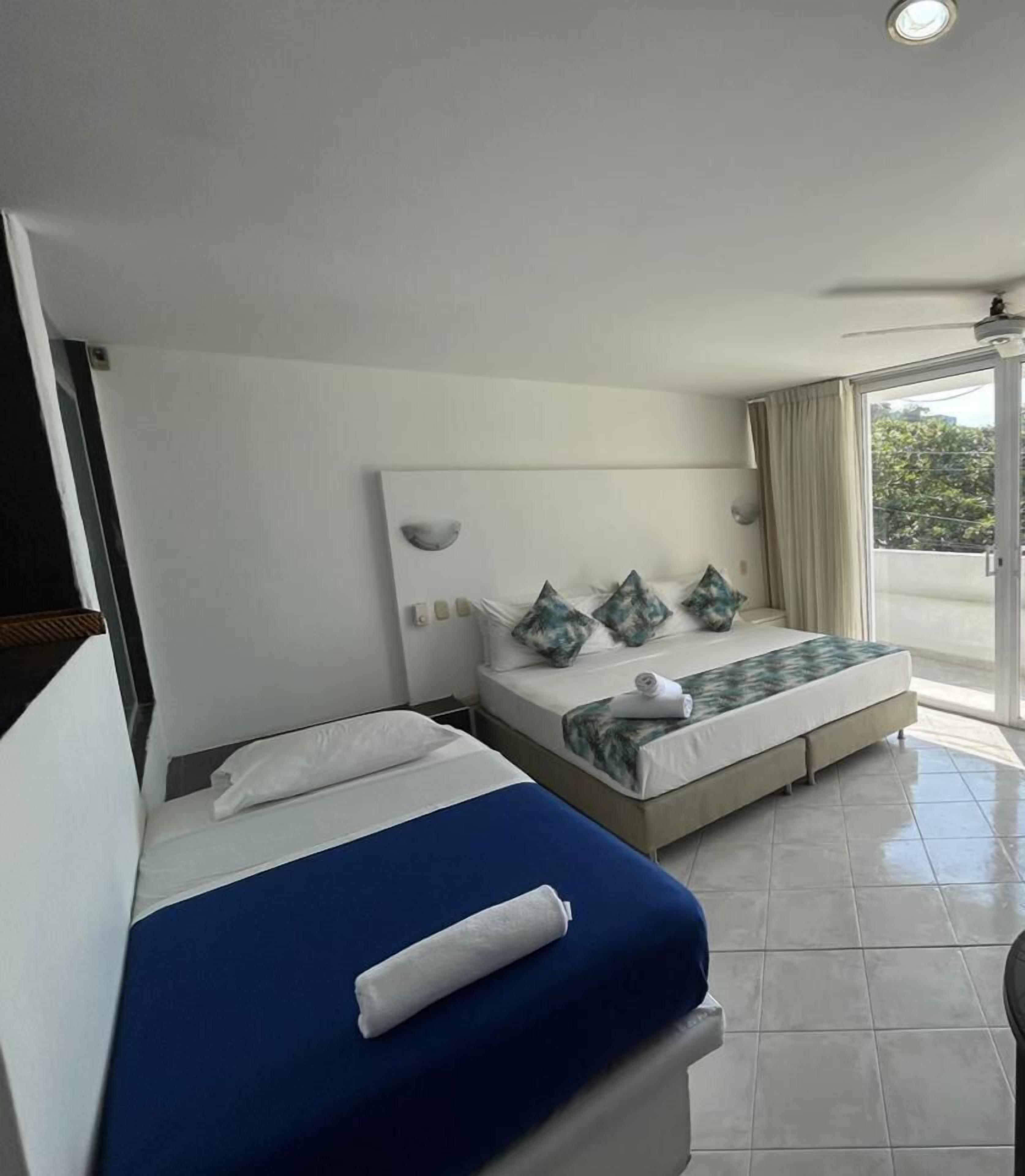 Quarto de hotel com duas camas, uma janela grande e um ventilador de teto.
