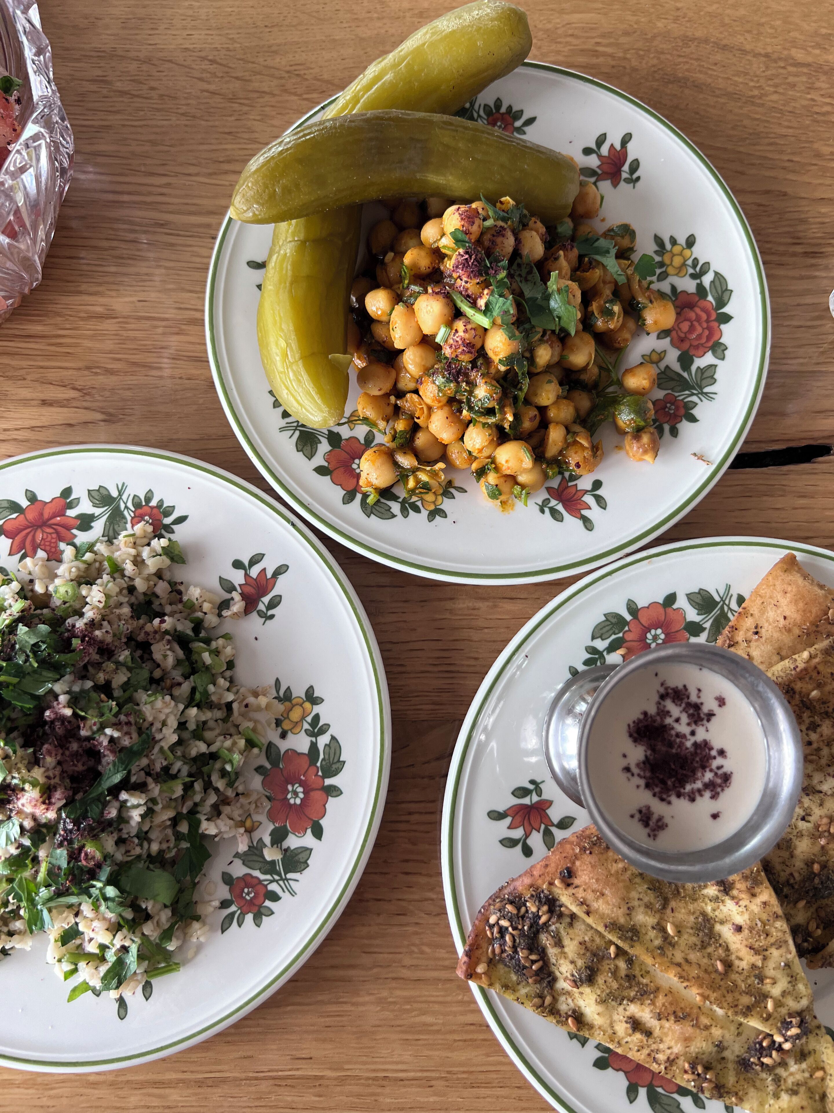 Uma mesa com diversos pratos, incluindo salada, grão de bico, picles e pão sírio.