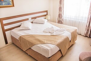 Cama bem arrumada com cabeceira de madeira, roupa de cama branca e manta marrom estampada.