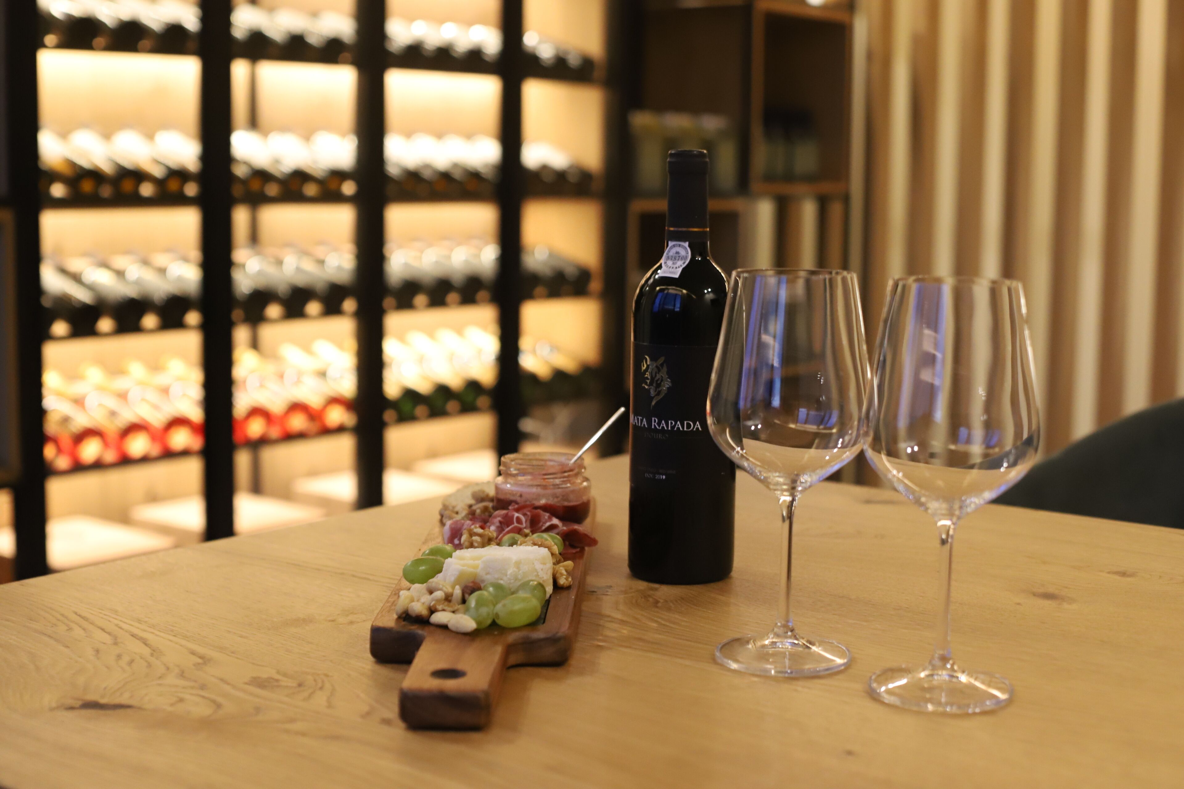 Uma mesa de madeira com uma garrafa de vinho, duas taças e uma tábua de frios.