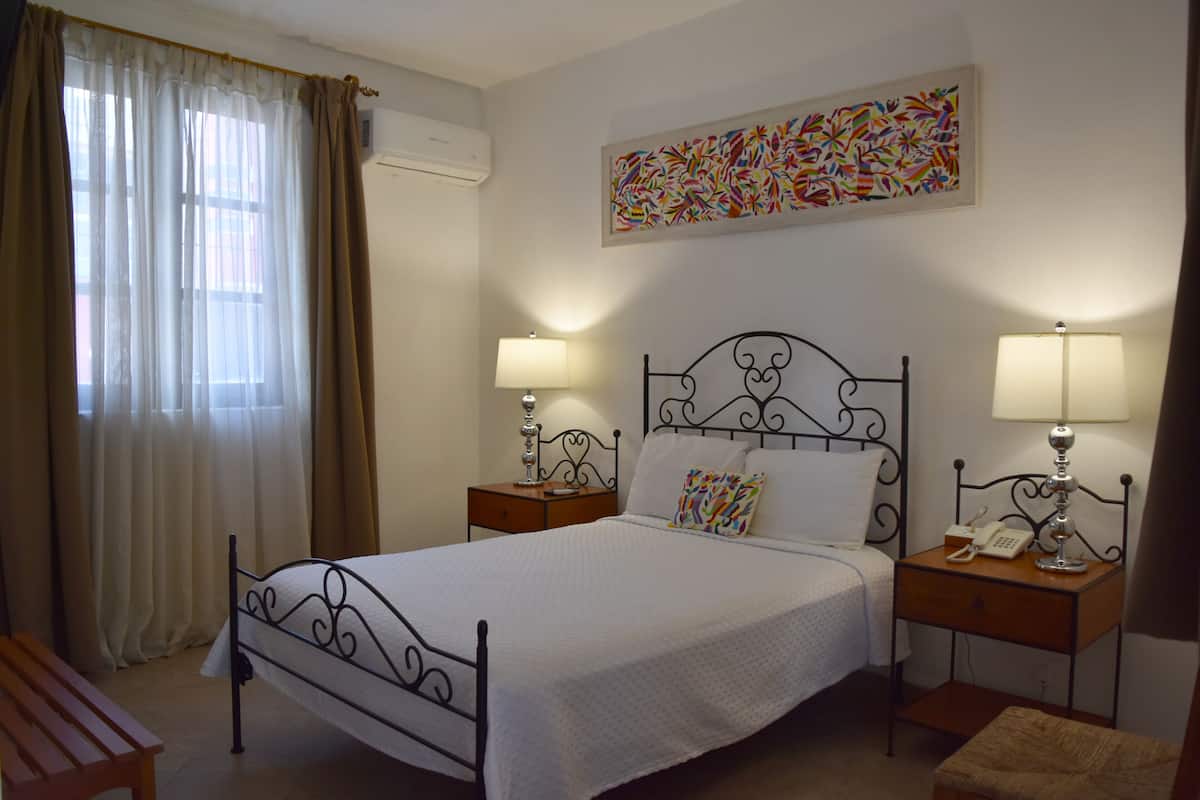 Quarto bem arrumado com cama, mesas de cabeceira, um banco e uma obra de arte colorida na parede.