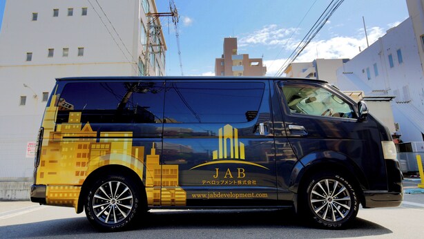 Uma carrinha escura com um desenho urbano e o texto "JAB Development Company" na lateral.