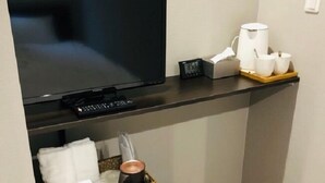 Quarto de hotel com televisão de tela plana, cafeteira, relógio e cesta com uma vela.