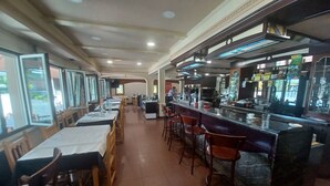 Restaurante com um balcão comprido, várias mesas e cadeiras.