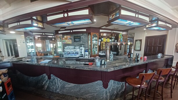 Uma área de bar com bancada de mármore, banquetas e uma máquina de café.