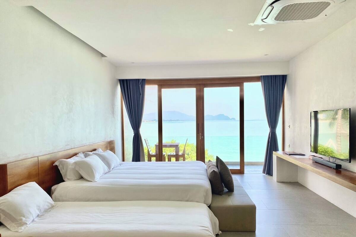 Quarto de hotel com duas camas, televisão e varanda com vista para o mar.