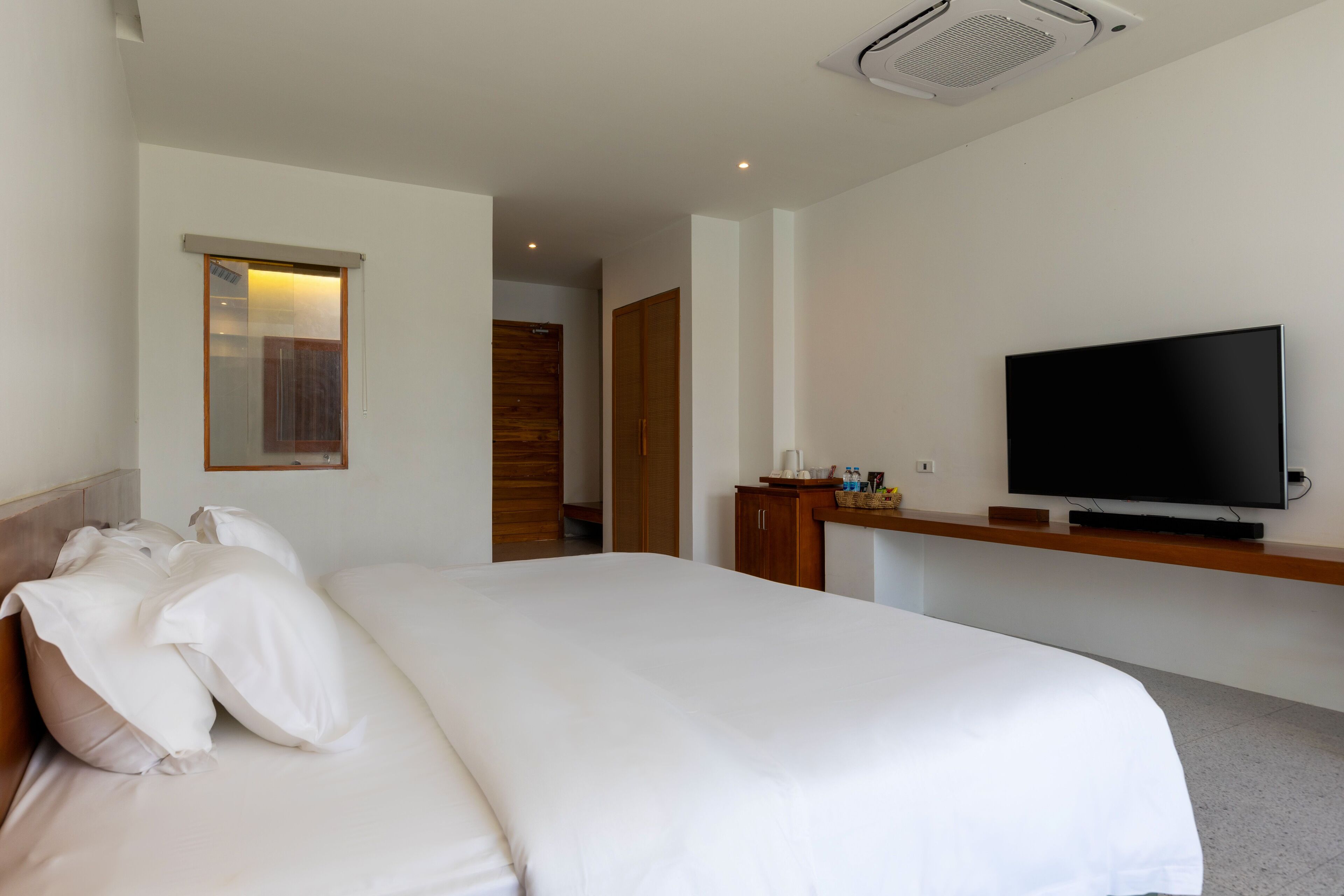 Quarto de hotel com uma cama grande, uma televisão sobre um suporte de madeira, um guarda-roupa e um espelho na parede.