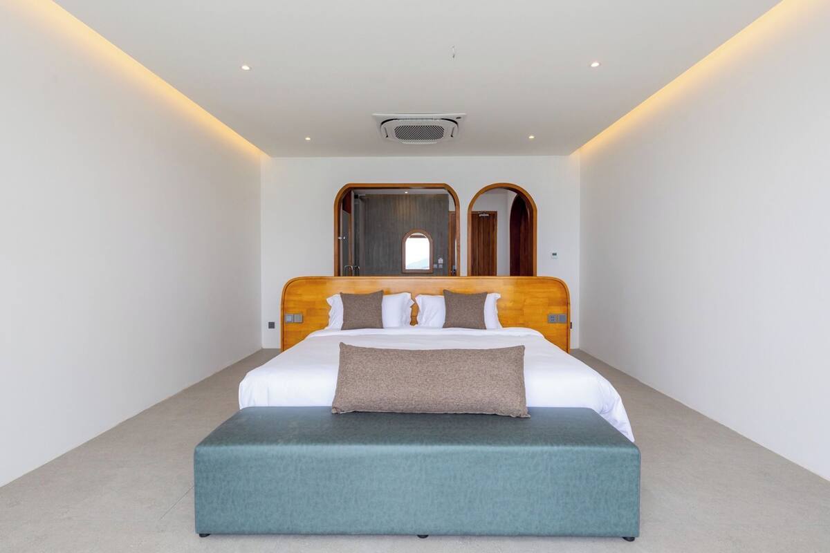 Quarto de hotel moderno com uma cama grande, cabeceira de madeira e um espelho amplo sobre a cama.