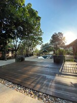 Um deck de madeira com piscina, cercado por árvores e plantas em vasos.