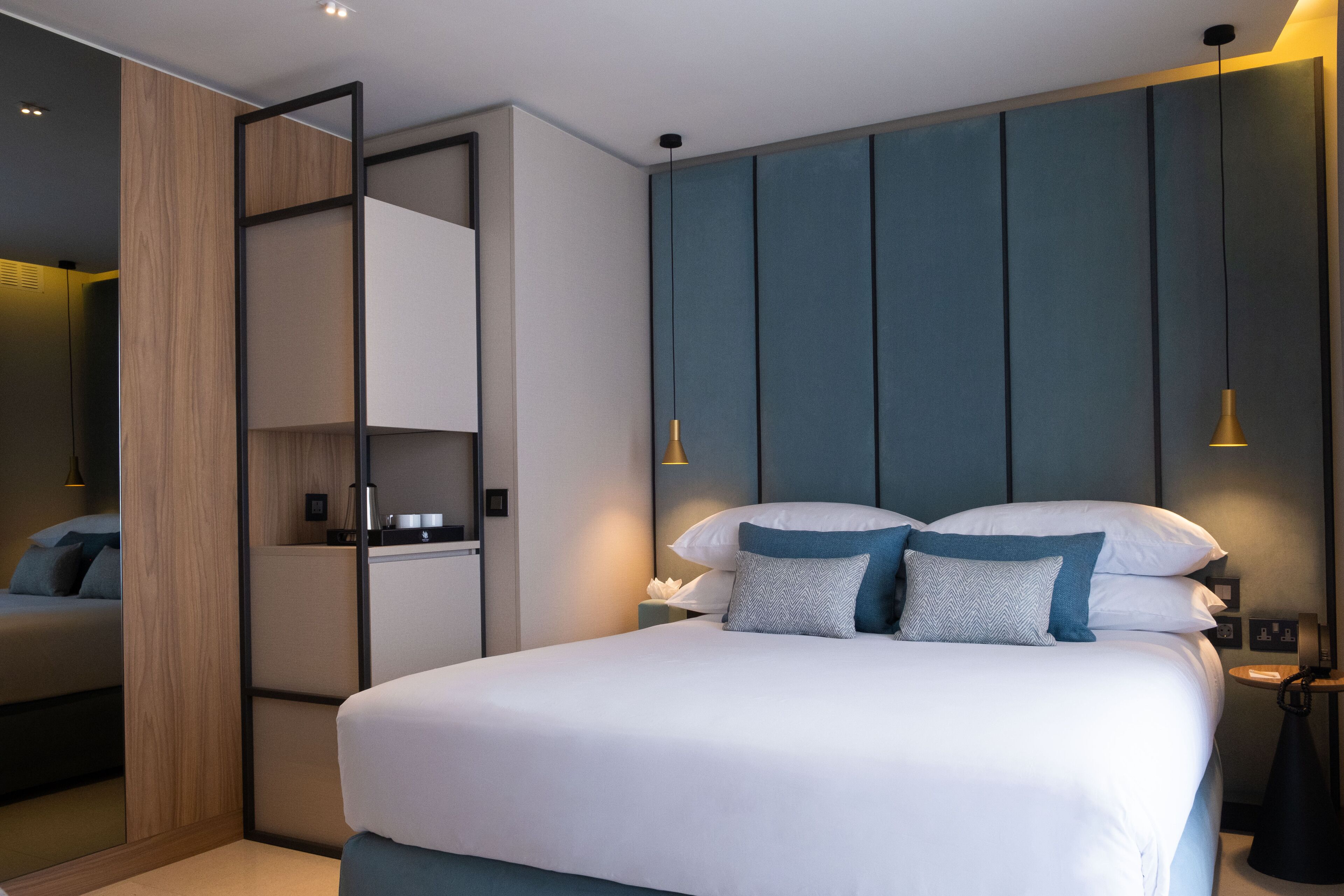 Quarto de hotel moderno com uma cama grande, guarda-roupa embutido e mesa de cabeceira com abajur.