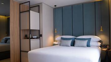 Quarto de hotel moderno com uma cama grande, guarda-roupa embutido e mesa de cabeceira com abajur.