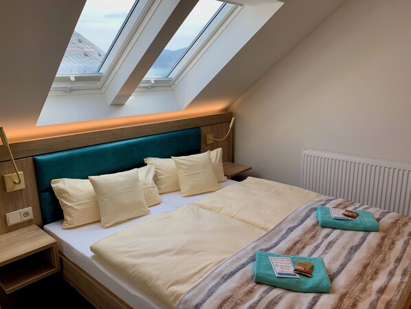 Quarto com claraboia, cama com roupa de cama branca, cabeceira verde-água e mesa de cabeceira com abajur.