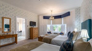 Quarto de hotel com duas camas, cômoda, televisão e janela com vista para o verde.