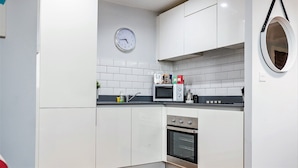 Uma cozinha moderna com armários brancos, micro-ondas, forno e um relógio na parede.
