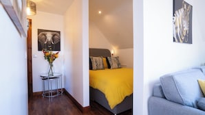 Um quarto com uma cama, um sofá cinza, um quadro de zebra fixado na parede e um vaso com flores.