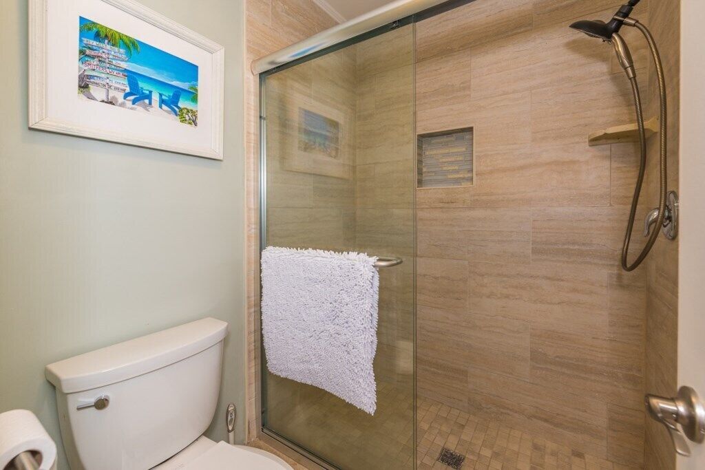 Casa de banho com cabine de duche em vidro, sanita e quadro pendurado na parede.