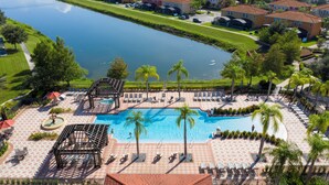 Um resort com piscina, espreguiçadeiras, palmeiras e vista para um lago.