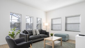 Uma sala de estar moderna com um sofá cinzento, uma mesinha e um banquinho azul.