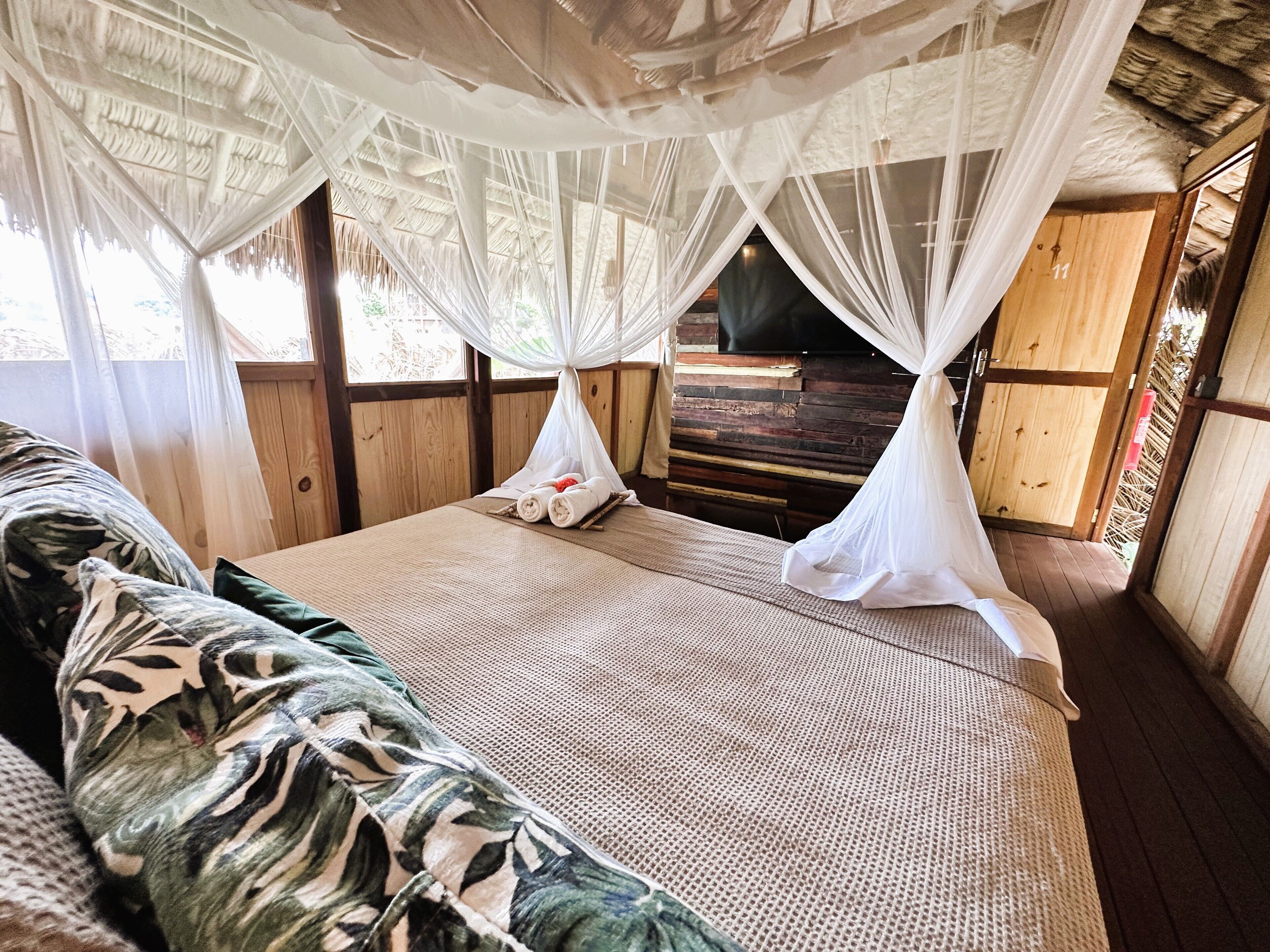 Quarto com cama, mosquiteiro e paredes de madeira.