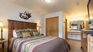 Quarto com uma cama grande, cabeceira de madeira, decoração de chifres de veado e uma toucador com espelho e iluminação.