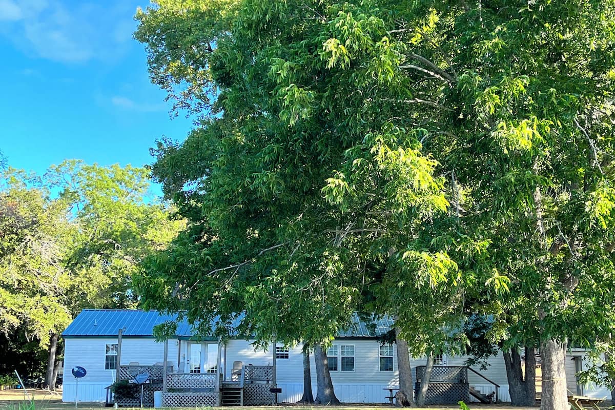 Uma casa branca com telhado azul, rodeada por árvores e um gramado.
