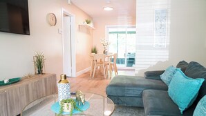 Uma sala de estar moderna com uma mesa de centro de vidro, um sofá cinza escuro e um espaço de jantar com mesa e cadeiras de madeira.