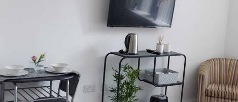 Uma sala de estar moderna com televisão na parede, um espaço de refeições com mesa e cadeiras, e uma poltrona listrada.