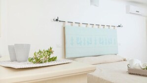 Quarto limpo e minimalista com uma cama, uma pequena mesa com xícaras e uma planta, além de um porta-toalhas fixado na parede.