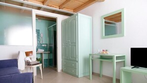 Um quarto com um sofá azul, um guarda-roupa verde, uma pequena mesa com um espelho e uma TV sobre um suporte.