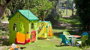 Uma área de recreação infantil com um parquinho verde, escorregadores e cadeiras coloridas.