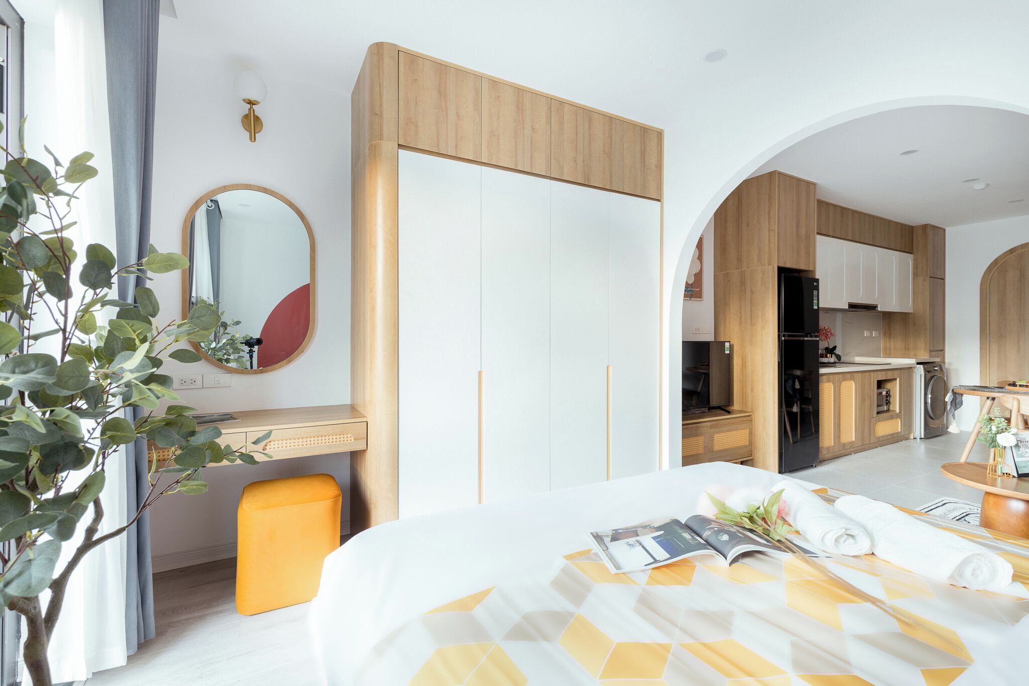 Quarto de hotel com uma cama, escrivaninha, espelho e vista para a área da cozinha.