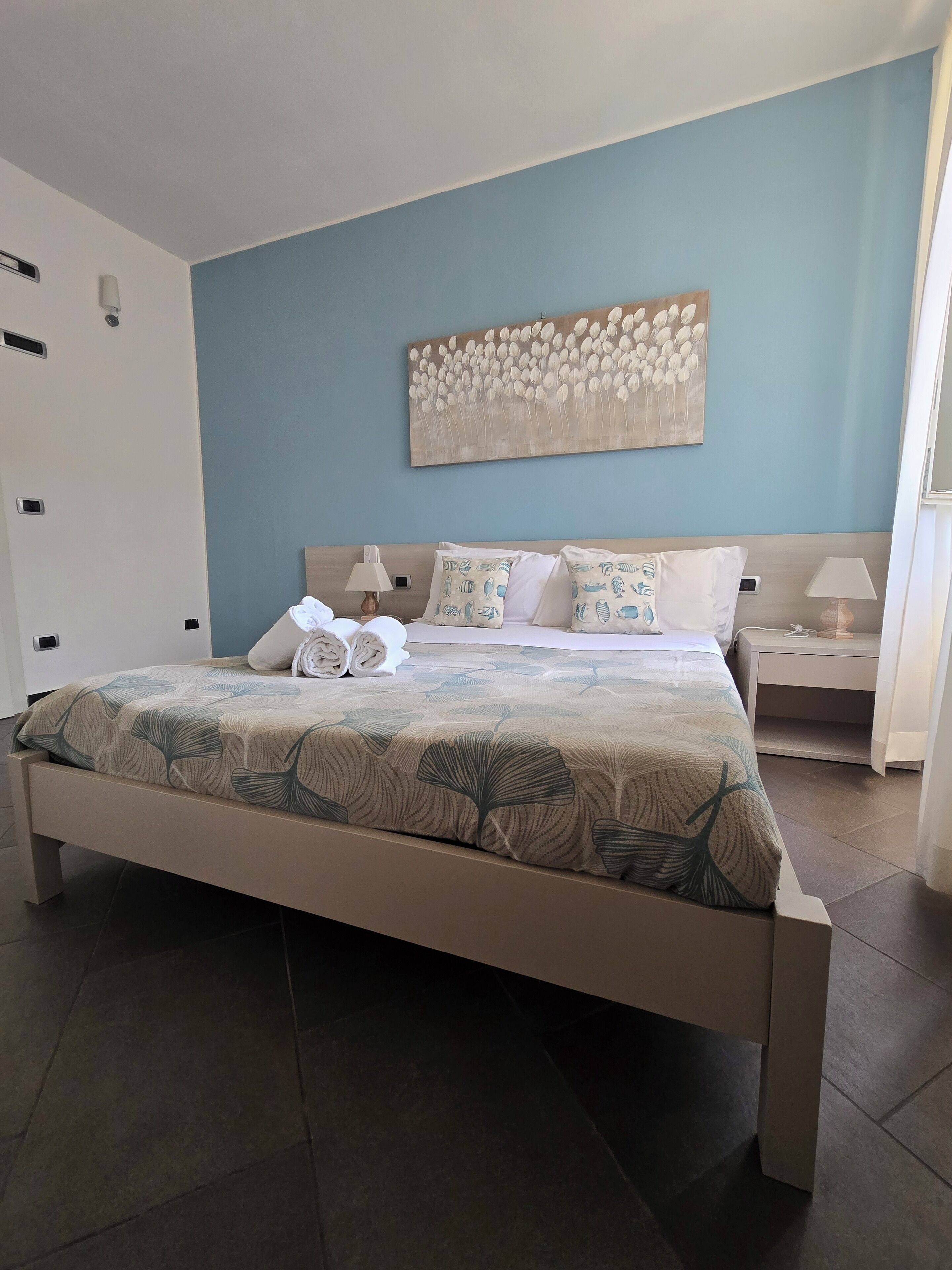 Quarto com cama, duas mesas de cabeceira, luminária na parede e um quadro.