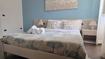Quarto com cama, duas mesas de cabeceira, luminária na parede e um quadro.