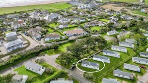 Vista aérea de uma área residencial costeira com casas, campos verdes e uma praia.