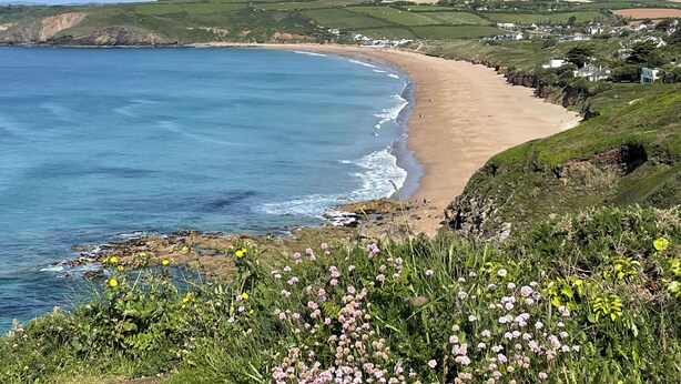 Paisagem costeira com uma praia arenosa, colinas gramadas e céu claro.