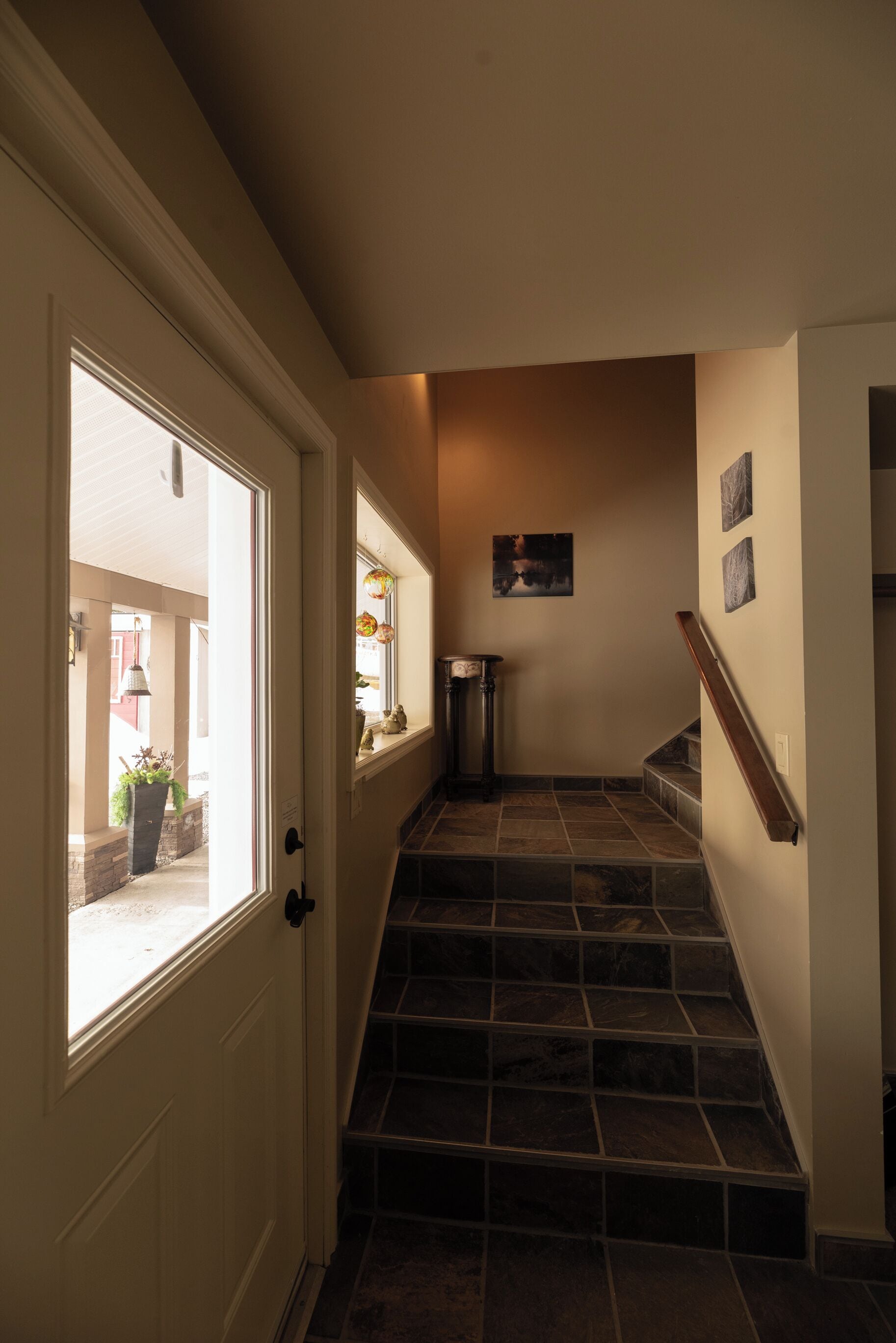 Uma escadaria com corrimão, uma porta com janela e um quadro fixado na parede.