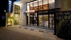 Entrada de hotel com design moderno, destacando grandes janelas de vidro e fachada de tijolos.