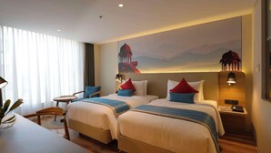 Quarto de hotel com duas camas, uma escrivaninha, uma cadeira e um mural grande na parede.