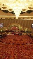 Um salão imponente com um grande candelabro, decorações florais e um palco com um sofá dourado.