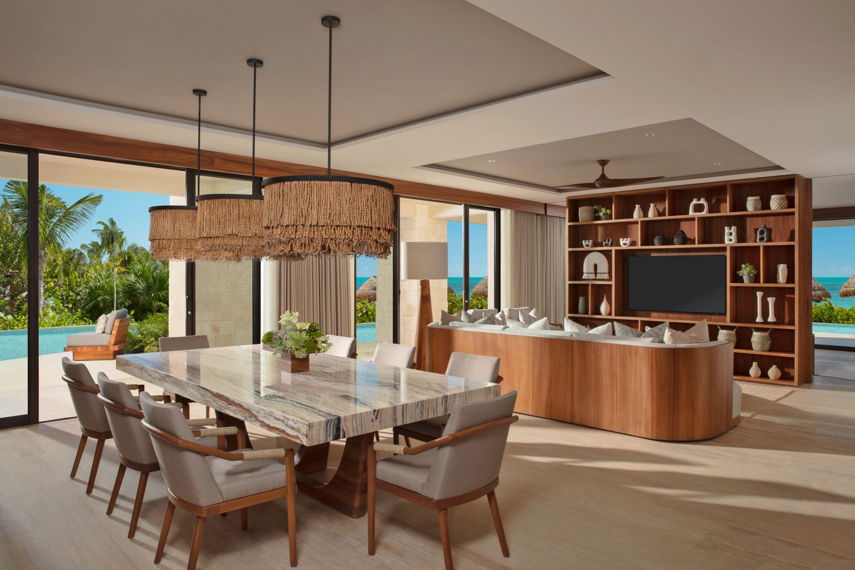 Uma sala de estar moderna com uma grande mesa de mármore, assentos confortáveis, um móvel de entretenimento de madeira e vista para o mar.