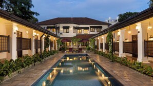 Uma área de piscina com uma piscina retangular alongada, ladeada por um caminho revestido de azulejos, e um edifício com várias janelas e varandas ao fundo.
