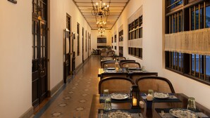 Um corredor com mesas e cadeiras de jantar, um candelabro e janelas com cortinas.